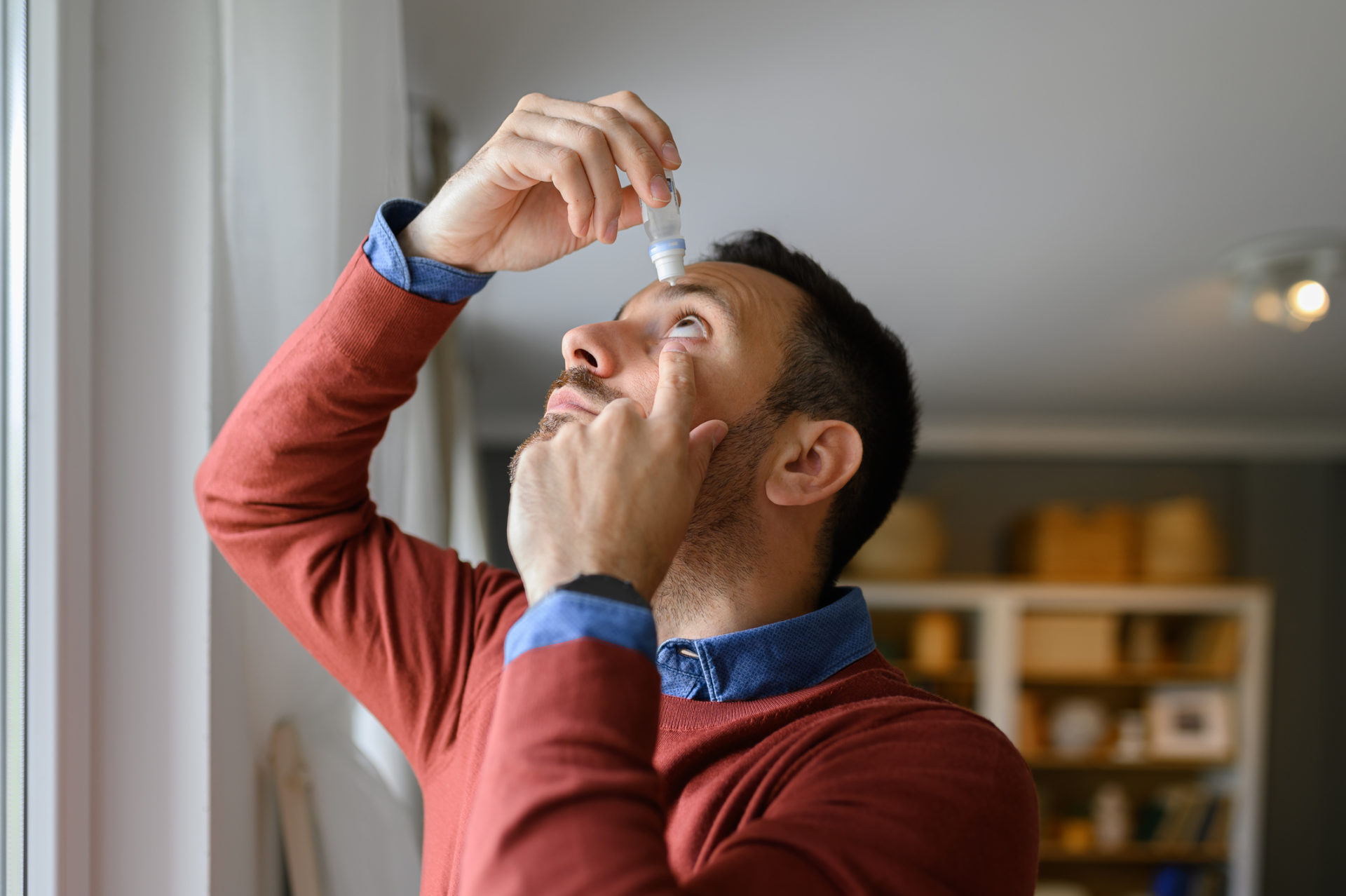 Close-up of young man applying eye drops to treat dry eye and ...